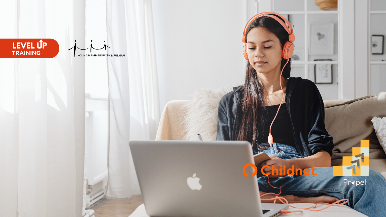 A young person comfortably sitting on a sofa wearing headphones and using their laptop ...